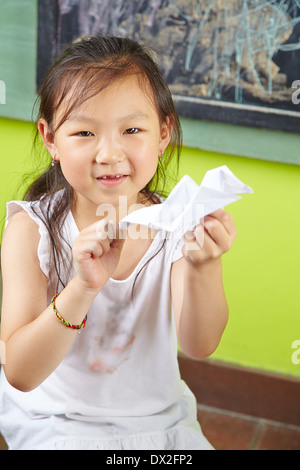 Little cute girl doing origami sitting at the table with a big window ...