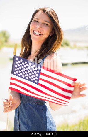 Laughing young woman with USA flag pointing at viewer on orange ...