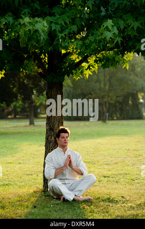 Young man meditating under a tree Stock Photo - Alamy