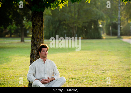 Young man meditating under a tree Stock Photo - Alamy