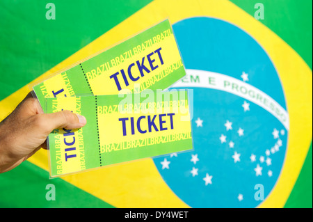 Hand holding two Brazil tickets against bright Brazilian flag ...