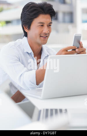 Happy relaxed man holding his mobile phone as he stands smiling at the ...