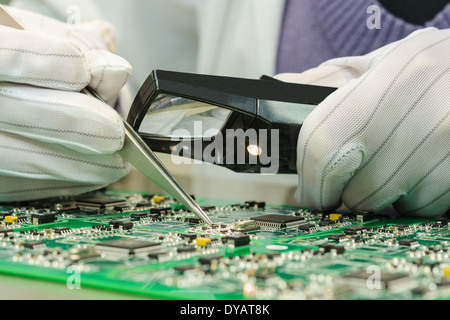 Woman in antistatic gloves holding pincette and magnifier repairing ...