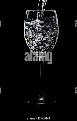 Crystal clear water being poured into a transparent glass with ice, creating refreshing ripples ...