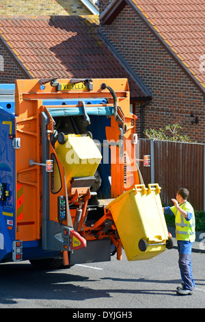 Dustman worker at back rear of refuse dustcart truck at work picking up ...