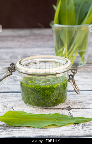 Preserving jar of wild garlic pesto on napkin and grey wooden table ...