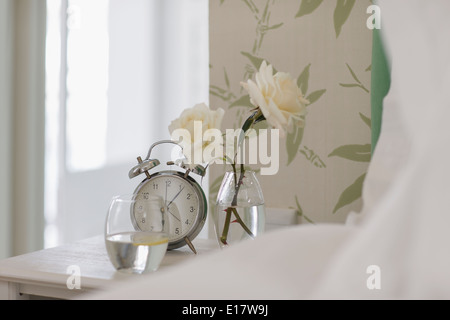 Clock and rose on bedside table near blurred man using smartphone on ...