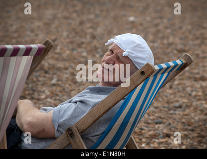 Using a knotted handkerchief as a sun hat a man rests in a deckchair on ...