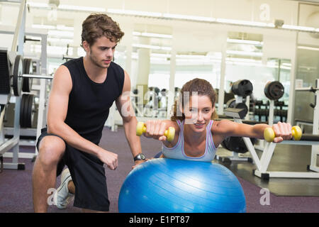 Trainer watching client balance on exercise ball with dumbbells Stock ...