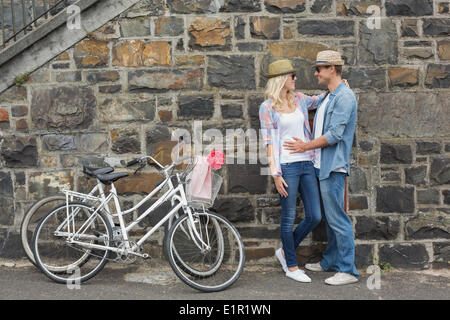 Hip young couple hugging by brick wall with their bikes on a sunny day ...