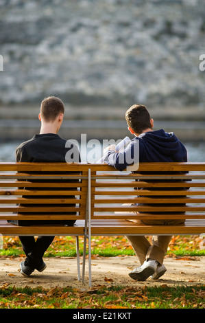 Two guys sitting on bench with hockey sticks and skates goal in back ...