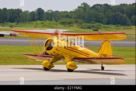 A yellow open cockpit Stearman biplane flies low over a small ...