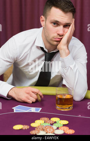 A young depressed male gambler at the gambling table gun and drugs in ...
