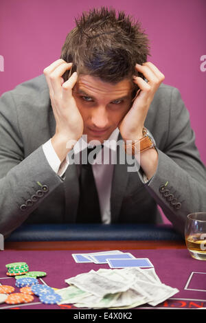 A young depressed male gambler at the gambling table gun and drugs in ...