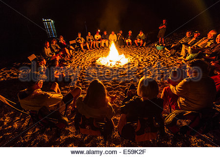People sitting at a camp fire, illuminated wall tent, cabin behind ...