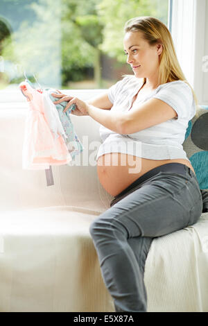 Pregnant woman preparing baby clothes and sitting on sofa at home Stock ...