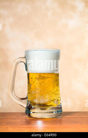 A glass mug filled with amber liquid sits on a wooden surface ...