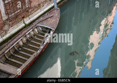 An old work boats moored along a side canal in Venice with reflections ...