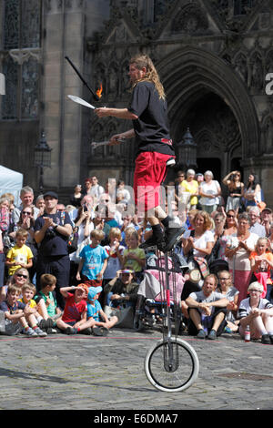Street performer juggling with fire on a unicycle watched by tourists ...