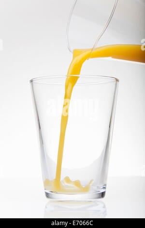 Orange juice pouring from jug into glass over color background with ...