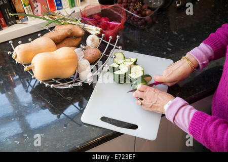 Woman chopping courgettes vegetables in the kitchen on a chopping board ...