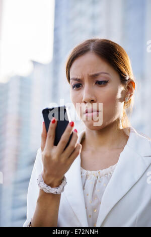 Businesswoman with disappointed expression using mobile phone in city ...