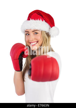 Festive blonde punching with boxing gloves against blurry christmas ...