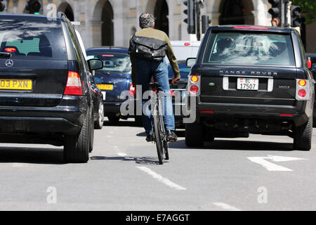 A cyclist cycling in London amongst a queue of traffic. Pedestrians ...