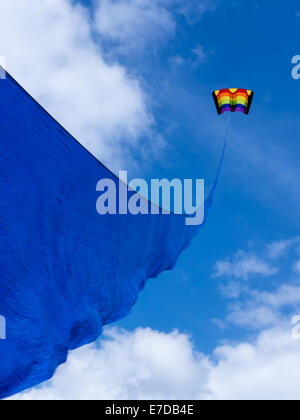 A multicolored kite flying against a blue sky on a beach side Stock ...