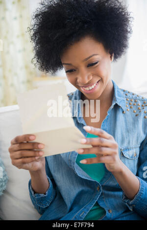 Young african american woman reading book sitting on bed at bedroom ...
