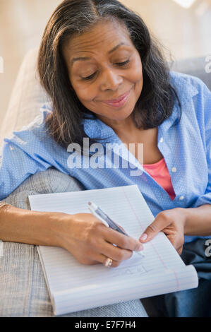 African american woman writing on notebook sitting on bed at bedroom ...