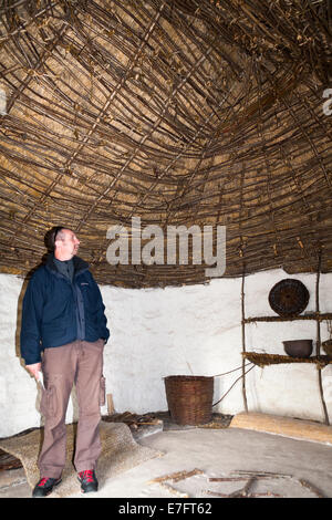 Tourist visitors thatched roof ceiling in recreated Neolithic stone age ...