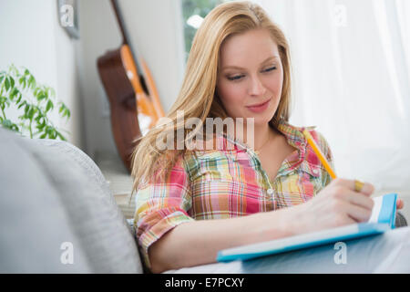 Blonde young woman writing down notes during yoga practice at home ...