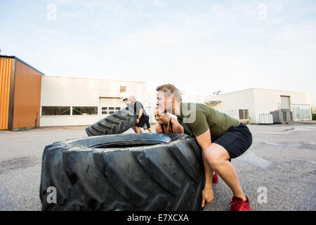 Fit athletes doing tire-flip exercise on sand. Horizontal extreame ...