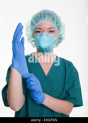 Young Asian female doctor in scrubs writing notes while using laptop ...