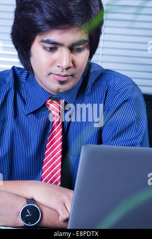 Serious Indian businessman sitting at the table in front of laptop ...