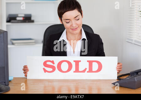 Real estate agent with a sold panel and houses miniatures in her office ...