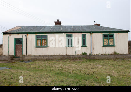an old, weathered prefab bungalow with green window frames and curtains ...
