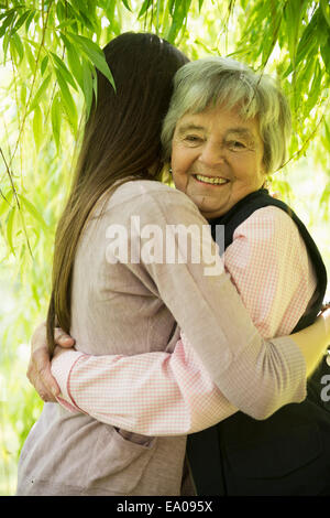Woman smiling under willow tree in sunlight with shadow from branches ...