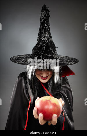 Tricky witch offering a poisoned apple, Halloween theme Stock Photo - Alamy