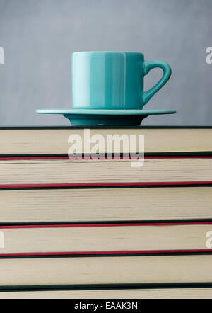 Ceramic cup and stack of books on wooden chair against white brick wall ...