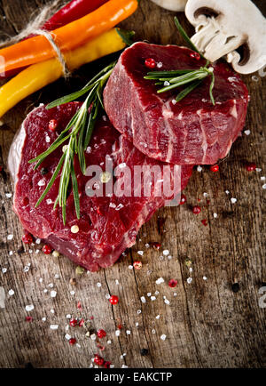 A fresh raw beef steak meat on a wooden board and vegetables on a table ...