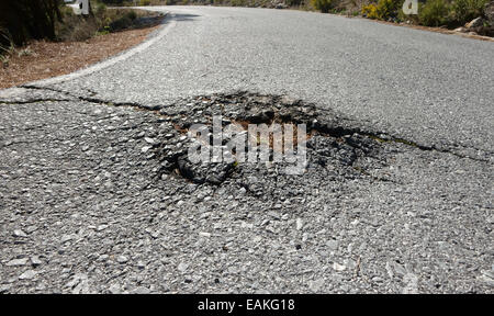 Low view of cracked tarmac lifted by tree roots road in mountains of ...