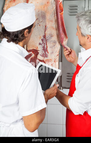 Butcher examining meat hanging in slaughterhouse Stock Photo - Alamy