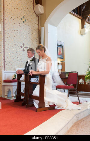 The bride and groom are kneeling during a wedding in the Catholic ...
