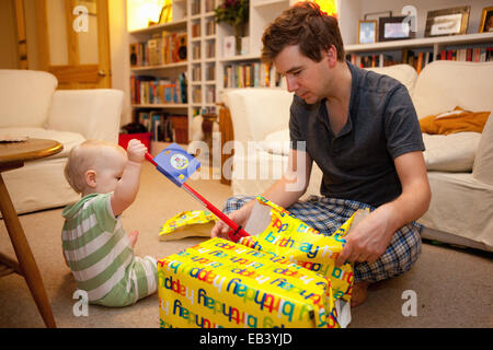 Cute baby boy with his father opening Christmas gifts on floor at ...