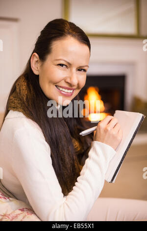 Woman writing Christmas to do list on notebook on colored background ...