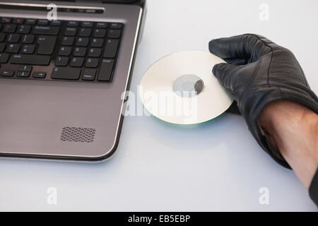 Burglar hacking and putting a cd-rom in laptop on white background ...
