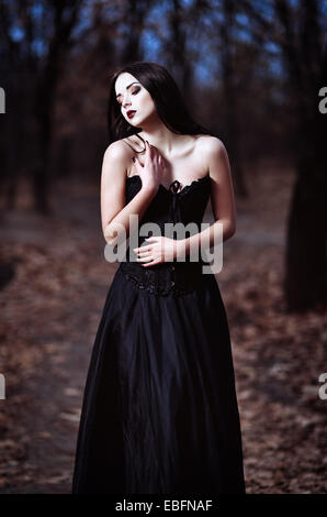 A beautiful sad goth girl stands in autumnal field. Grunge texture ...