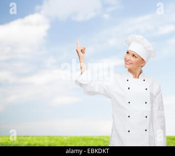 Happy female chef pointing at something on light grey background. Space ...